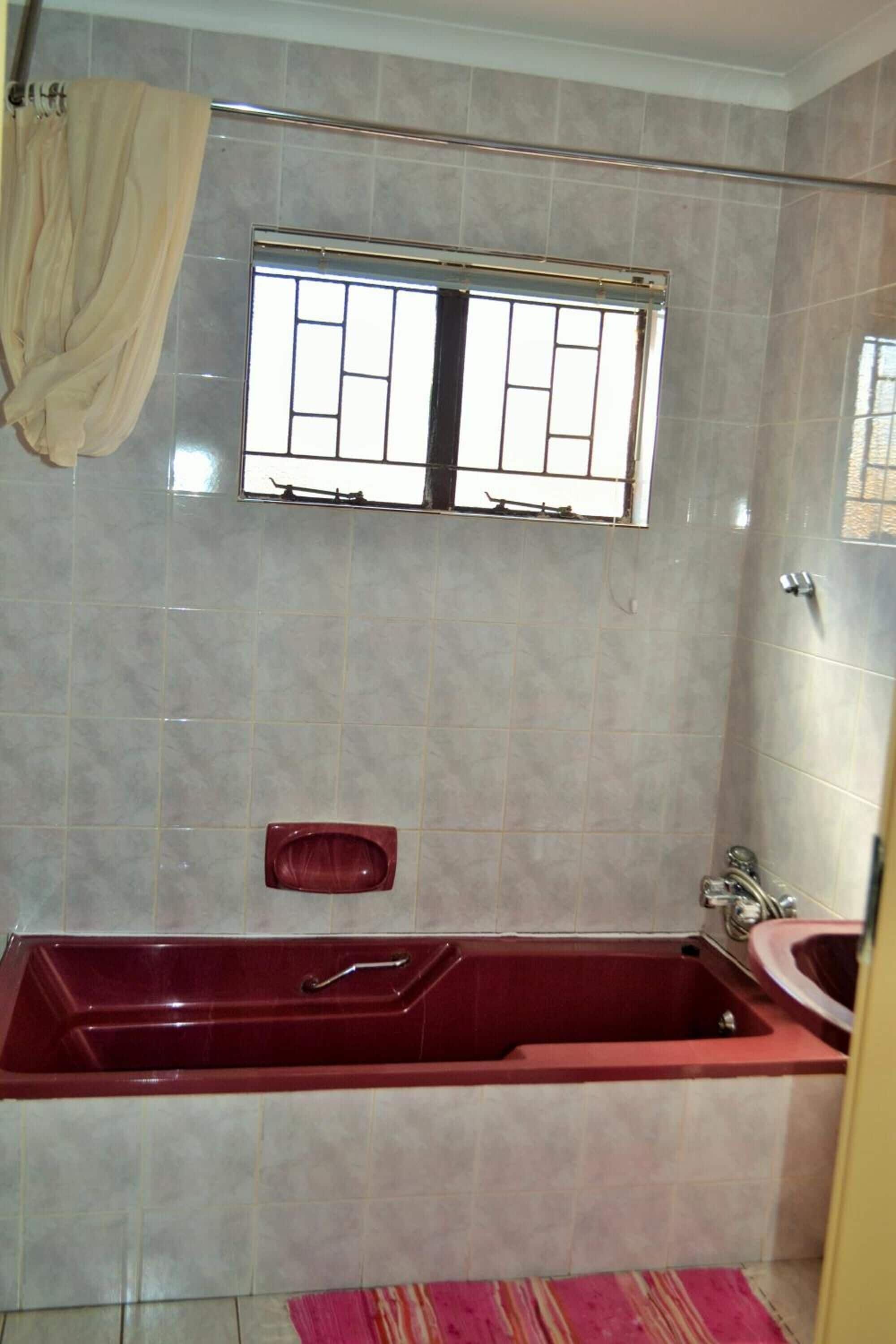 Casa de banho com banheira vermelha, janela com grades e área de duche.