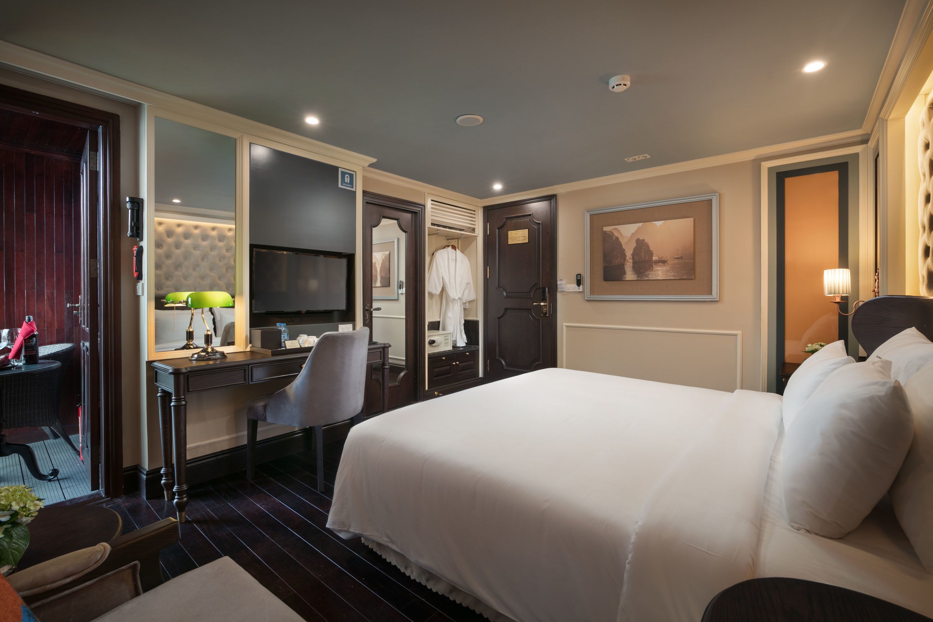 Quarto de hotel com uma cama grande, uma escrivaninha com cadeira, uma televisão e um espelho.
