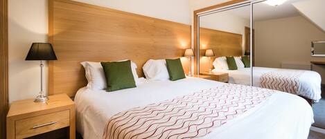Quarto de hotel com uma cama grande, uma mesa de cabeceira, um espelho e um abajur.