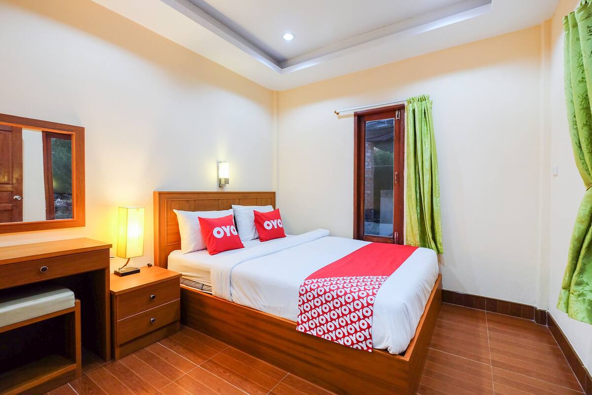 Um quarto com uma cama de madeira, uma mesa de cabeceira com abajur, uma escrivaninha e um espelho.