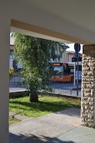 Ponto de ônibus com um pilar de pedra, cerca de metal e uma árvore ao primeiro plano.