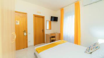 Quarto de hotel com cama, escrivaninha, cadeira, televisão e porta de banheiro.