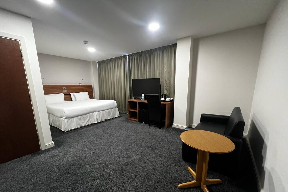 Quarto de hotel com cama, televisão, escrivaninha e mesa redonda pequena.