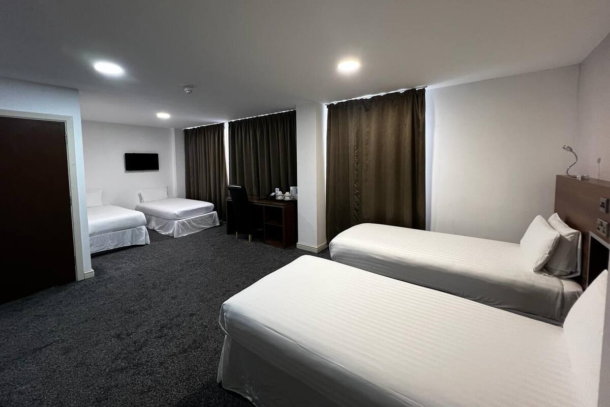 Quarto de hotel com duas camas de solteiro, uma escrivaninha com cadeira, TV de tela plana e chuveiro.