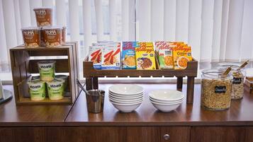 Buffet de café da manhã com diversas caixas de cereais, tigelas e recipientes de mingau e granola.