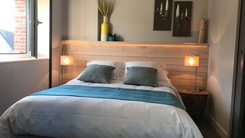 Quarto moderno com cabeceira de madeira, duas luminárias de apoio, cama grande com almofadas estampadas e uma obra de arte na parede.