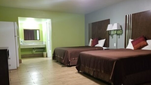Quarto de hotel com duas camas, uma kitchenette pequena e um banheiro visível através de uma porta aberta.