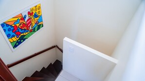 Uma escada com corrimão, uma obra de arte colorida na parede e um interruptor de luz.