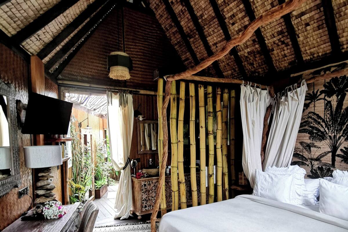 Quarto com cama, escrivaninha, cadeira, televisão e janela com cortinas.