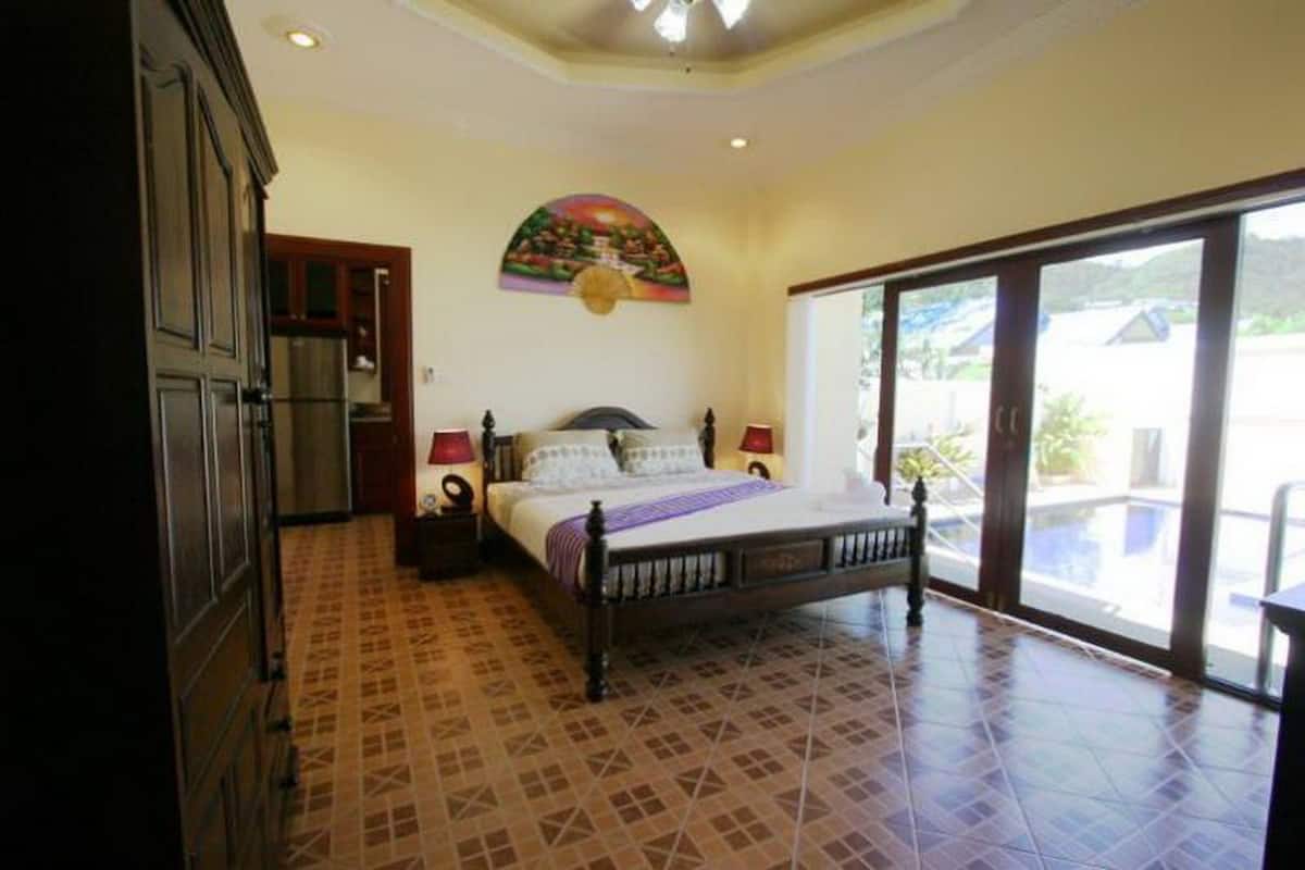 Quarto com cama, mesa de cabeceira, luminária na parede e uma janela grande com vista para o exterior.
