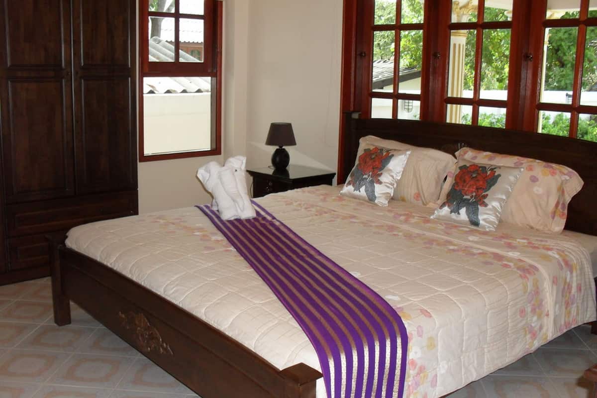 Cama bem arrumada com colcha florida, manta roxa e dois travesseiros com estampas florais.