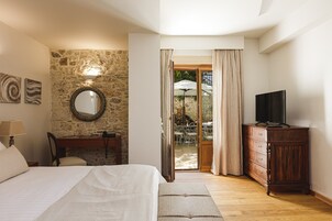 Quarto com cama, escrivaninha, cômoda, televisão e parede de pedra.