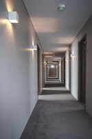 Um corredor comprido e estreito, com piso revestido de carpete e paredes em tons claros.