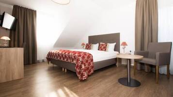 Quarto de hotel moderno com cama, escrivaninha, cadeira e mesa redonda.