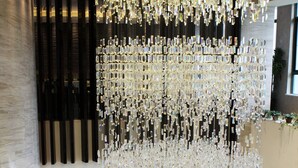 Um hall amplo com um lustre grande e ricamente decorado, uma área de estar com um tapete estampado e um vaso de planta.