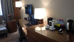 Quarto de hotel com escrivaninha, duas luminárias, televisão, cafeteira e minibar.