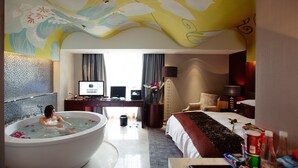 Quarto de hotel com uma banheira grande, uma escrivaninha com computador, uma cama com cobertor vermelho e uma TV na escrivaninha.