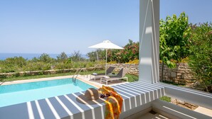 Área na piscina com vista para o mar, uma cadeira de lounge, um guarda-sol e um chapéu na borda.
