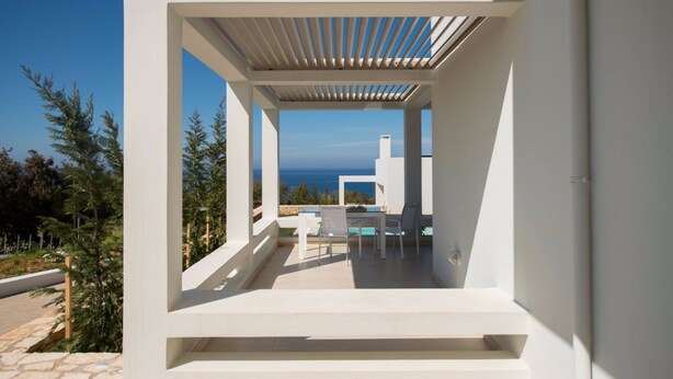 Um pátio moderno ao ar livre com vista para o mar, mobiliário branco e uma estrutura de pérgola.