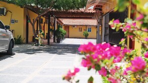 Uma rua estreita com edifícios amarelos, um carro estacionado e vasos de plantas.