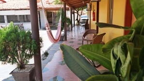Área externa coberta com rede, cadeiras e plantas em vasos.
