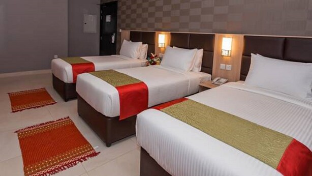 Quarto de hotel com duas camas, parede xadrez e um tapete pequeno.
