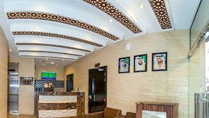 Um hall de hotel com balcão de recepção, área de estar e parede com quadros.
