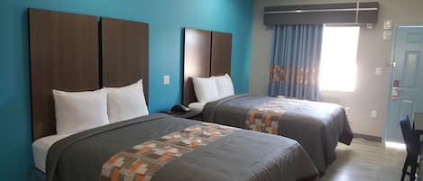 Quarto de hotel com duas camas, uma parede azul e uma janela com cortinas.