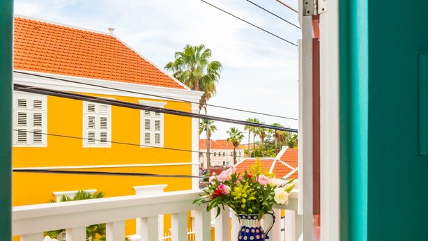 Uma varanda com guarda-corrimão branco, uma cadeira dobrável verde e uma mesa pequena com um vaso de flores.