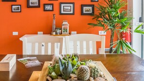 Uma sala de jantar com uma mesa de madeira, quadros nas paredes e um vaso de planta.