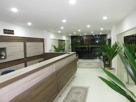 Uma área de recepção com balcão, plantas em vasos e uma placa indicando a recepção.