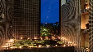 Um banheiro com banheira rodeada por velas, janela com vista para prédios e paredes revestidas de azulejos.