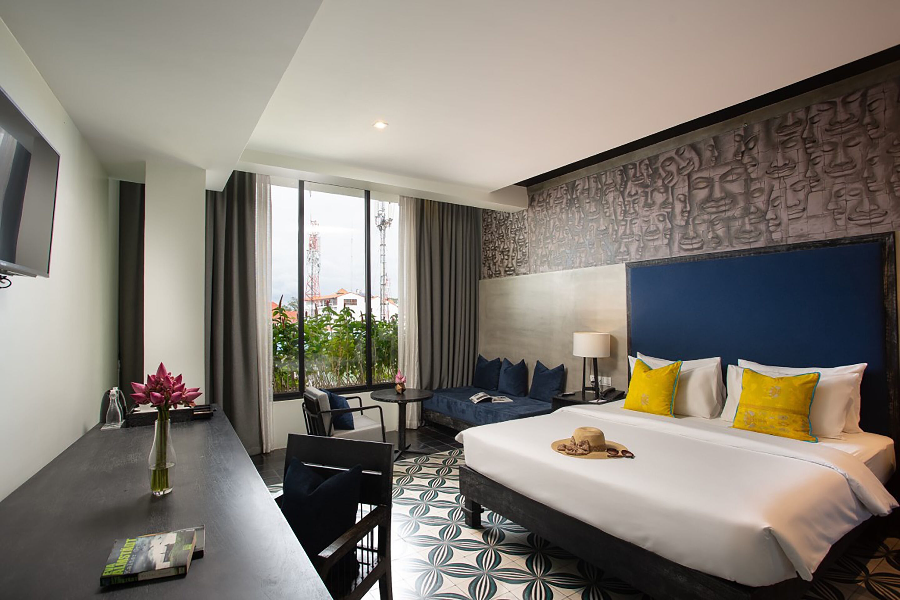 Quarto de hotel com cama, escrivaninha, cadeira, televisão e vista para o exterior.