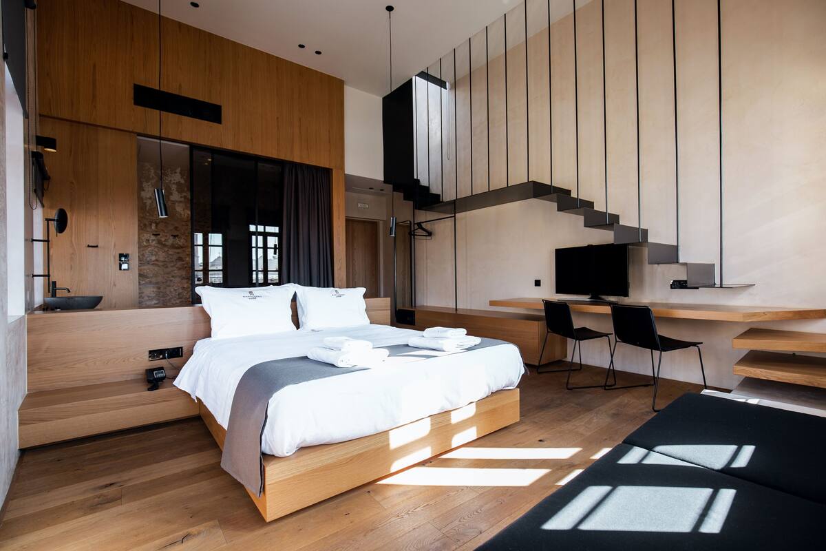 Quarto moderno com cama de madeira, escrivaninha e escada.
