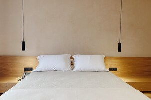 Cama bem arrumada com lençóis brancos e duas almofadas, cabeceira de madeira e telefone ao lado da cama.