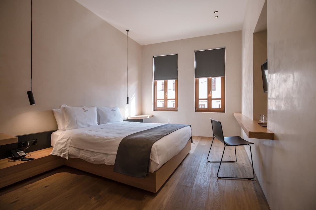 Quarto moderno com uma cama grande, mesas de cabeceira, uma cadeira e um espaço para trabalho.