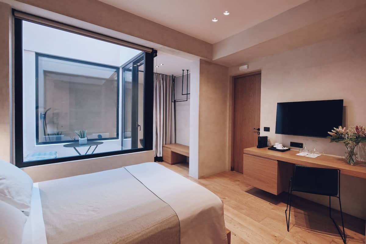 Quarto de hotel moderno com uma cama grande, uma escrivaninha, uma TV e vista pela janela.