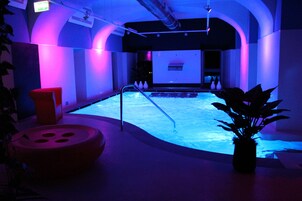 Uma área de piscina com borda curva, uma cadeira vermelha e um vaso com planta.