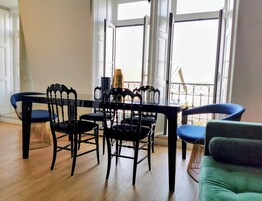 Uma sala de jantar com mesa e cadeiras, vista para a varanda externa e um sofá verde.