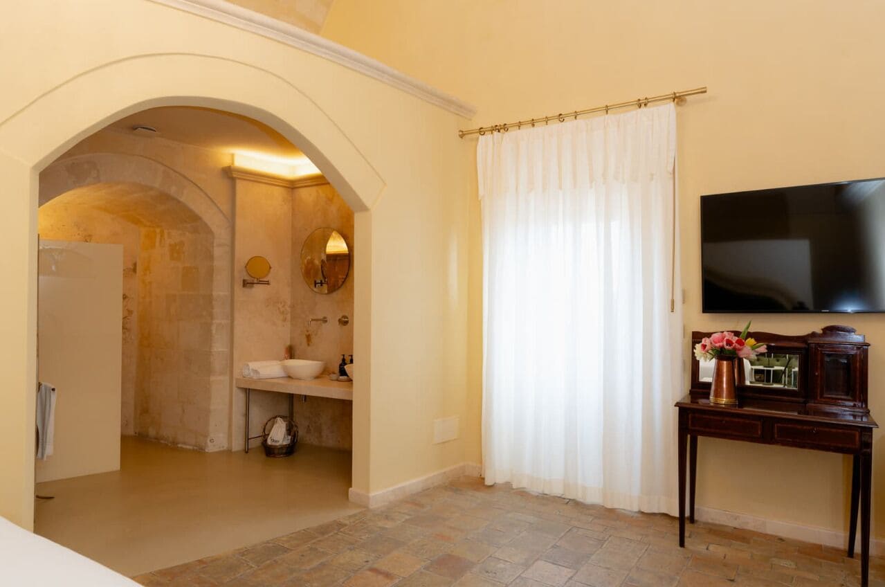 Casa de banho com arco de pedra, uma pia, um espelho e uma televisão sobre um suporte de madeira.