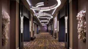 Um corredor comprido e estreito com carpete estampado, luminárias modernas e obras de arte abstratas nas paredes.