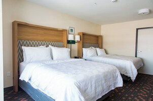 Quarto de hotel com duas camas, mesa de cabeceira, luminária e porta.