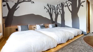 Quarto moderno com uma cama grande, duas mesas de cabeceira e um mural de árvores na parede.