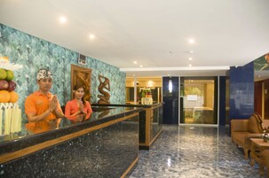 Área de recepção de hotel com chão de mármore, balcão de atendimento e parede com exposição de frutas.
