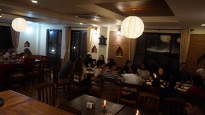 Um restaurante com mesas e cadeiras de madeira, lanternas de papel penduradas e paredes de tijolo.