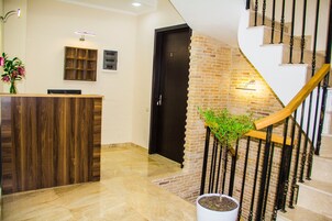 Uma área de recepção com uma mesa de madeira, uma porta preta e uma escadaria com parede de tijolos.