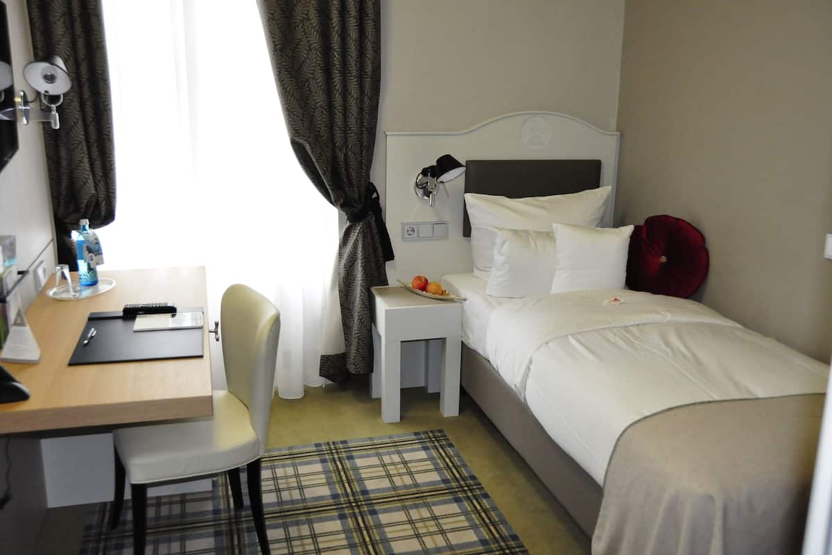 Quarto de hotel com cama, escrivaninha e cadeira, mesinha com bandeja de frutas, luminária e cortinas.
