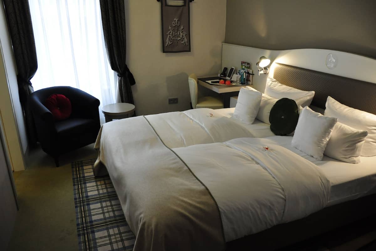 Quarto de hotel com uma cama grande, uma escrivaninha pequena, uma cadeira e uma mesa de cabeceira com abajur.