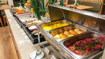 Buffet com diversos alimentos, incluindo carnes, batatas e outros pratos, dispostos em bandejas de metal.