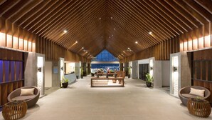 Um hall amplo com teto de madeira alto, áreas de estar confortáveis e vista para a cidade através de uma grande janela.